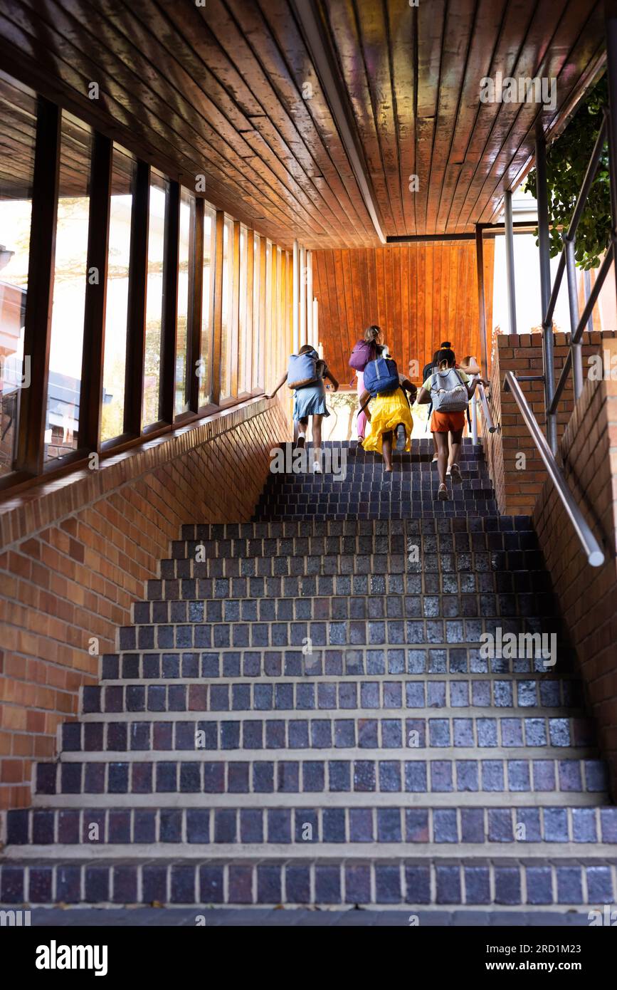 Diverse schoolgirls with bags running in elementary school staircase ...