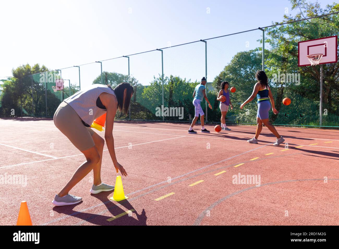 Diverse group of women setting cones and playing basketball at ...