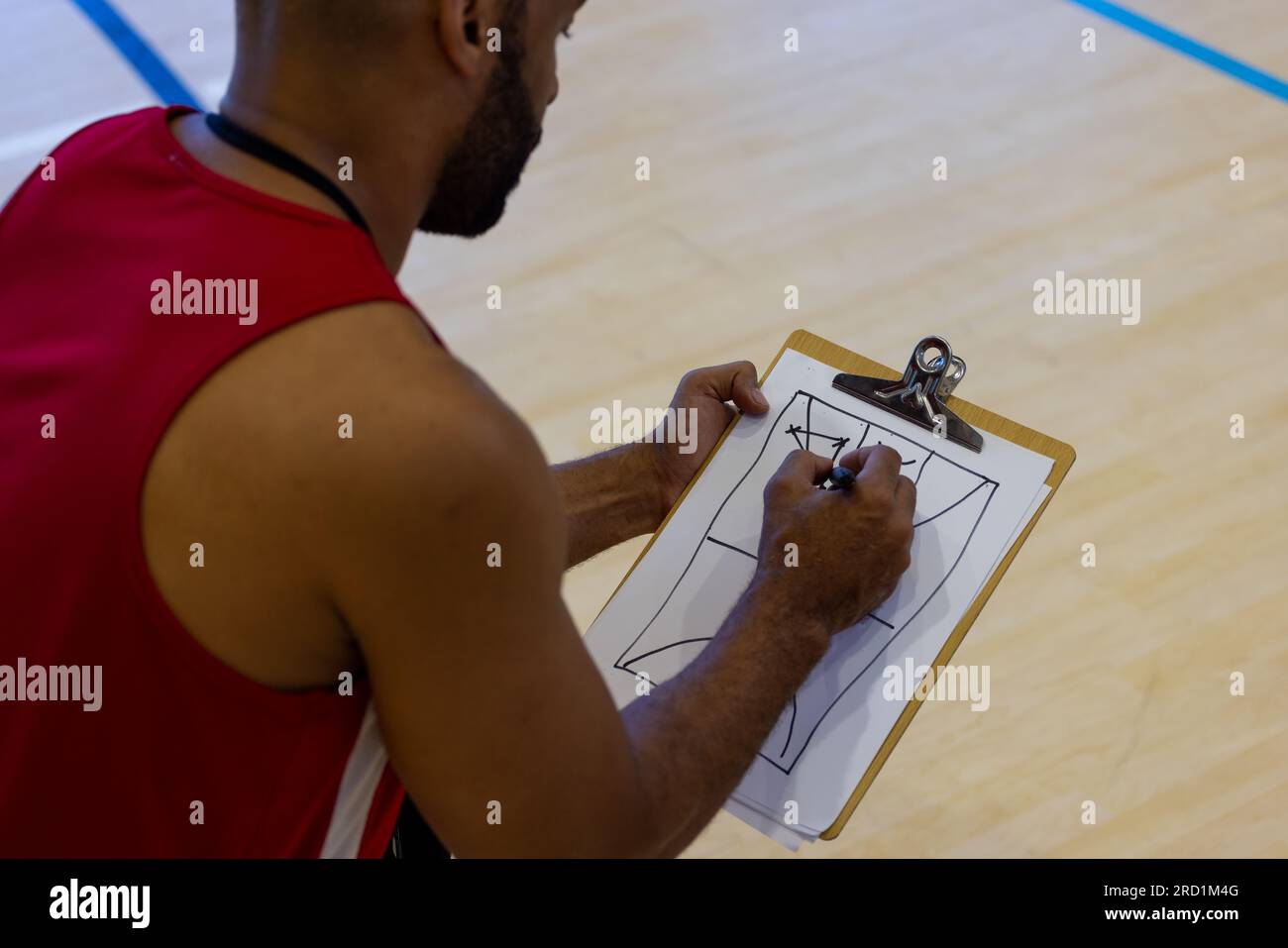 Biracial male coach holding clipboard and writing game plan at gym ...