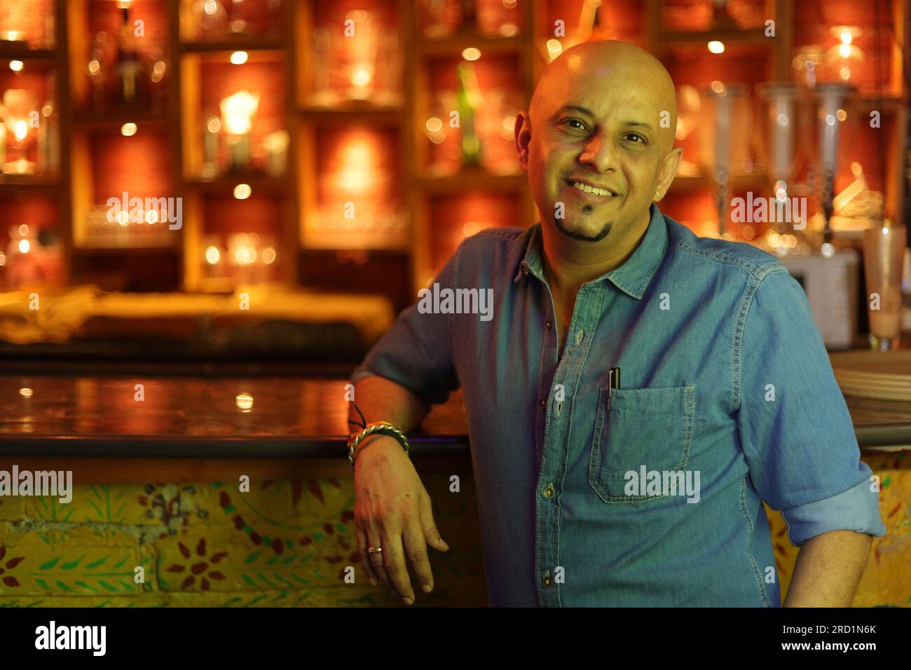 Young and flamboyant handsome bald guy standing on bar counter ...