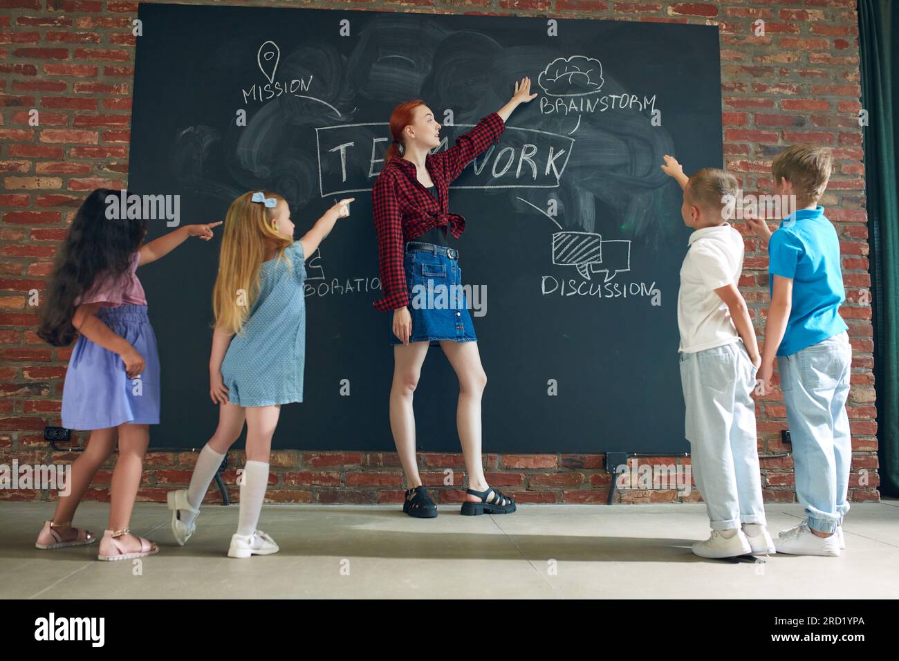 Young woman in casual clothes teaching kids to work together. Teamwork ...