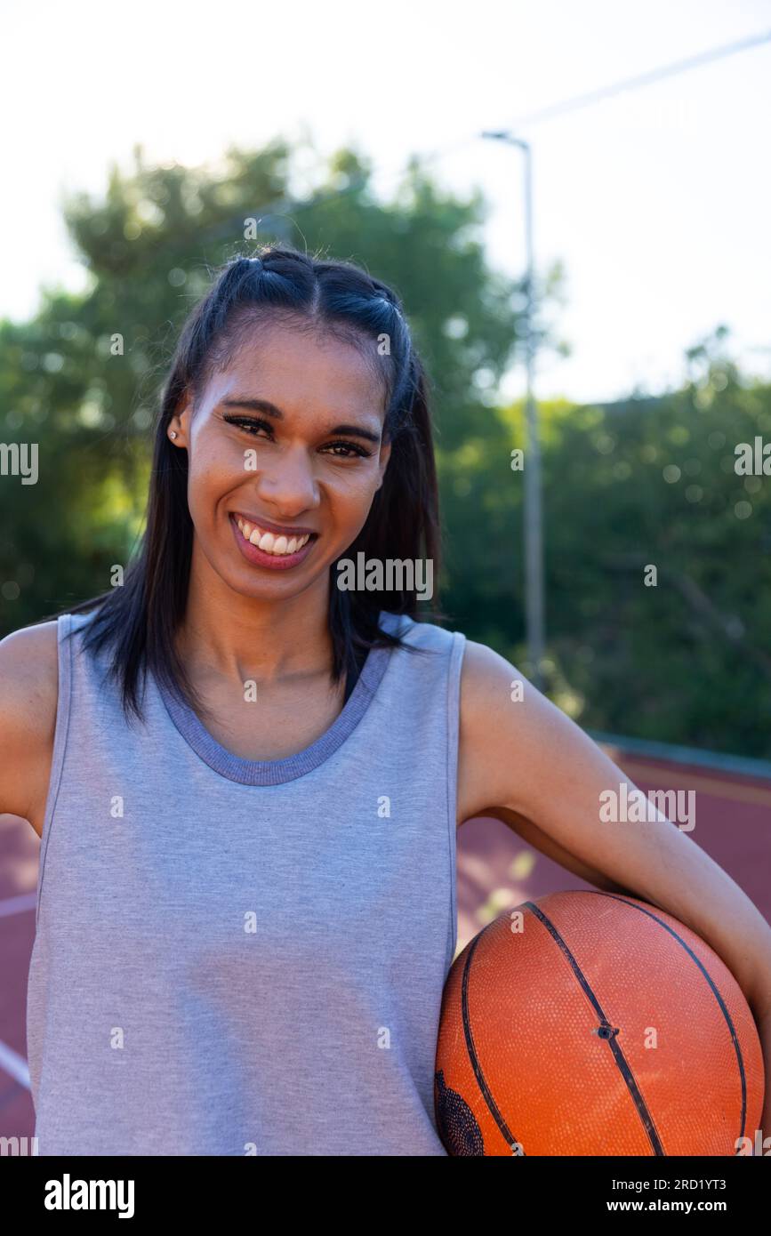 Portrait of happy biracial female basketball player holding basketball ...