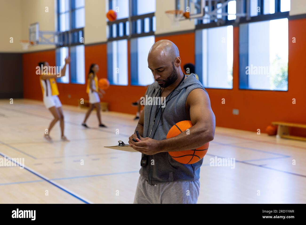 Biracial male coach writing on clipboard over female basketball players ...