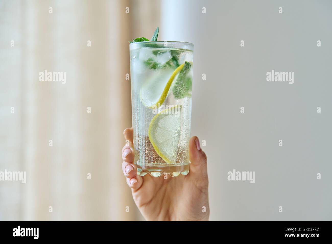 Cool drink mineral water with ice lemon mint leaves in woman's hand ...