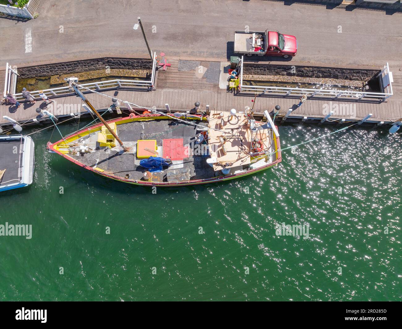 Aerial view of a fishing boat tied to a dock with a utility parked ...