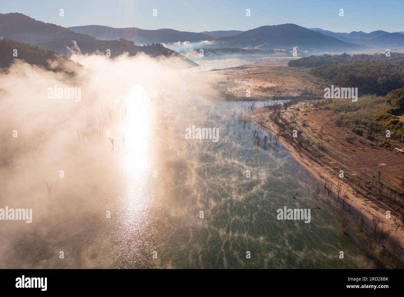 Aerial view of fog patches around the shoreline of a lake surrounded by ...