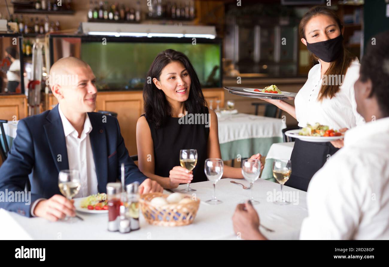 positive female busboy in mask severing order to friends in modern ...
