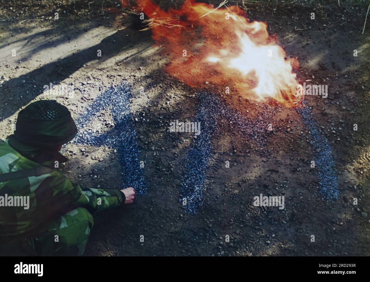 A conscript setting fire to gunpowder on the ground with the letters AM ...