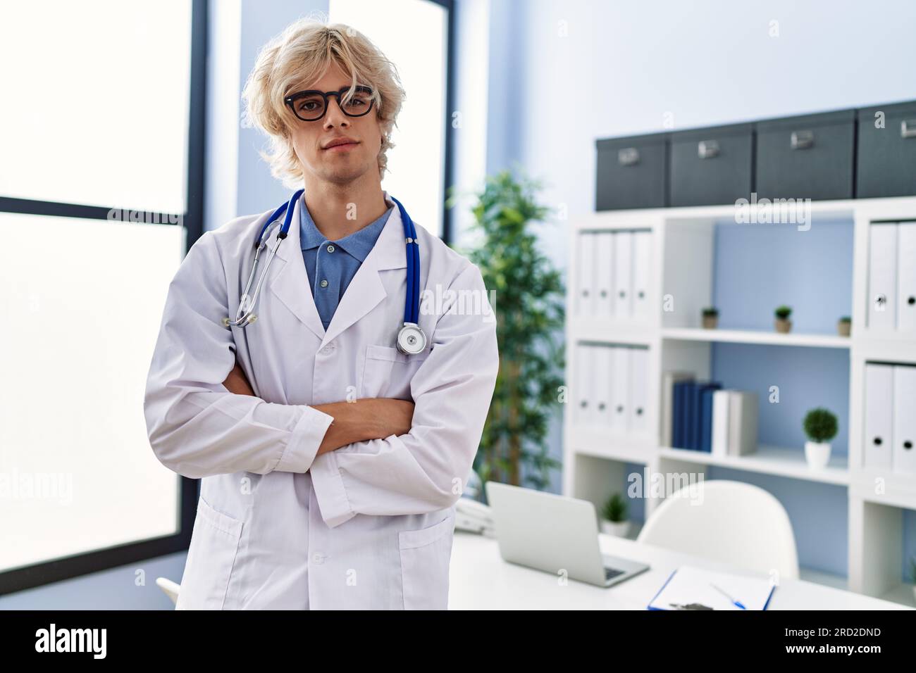 Young blond man doctor standing with arms crossed gesture at clinic ...