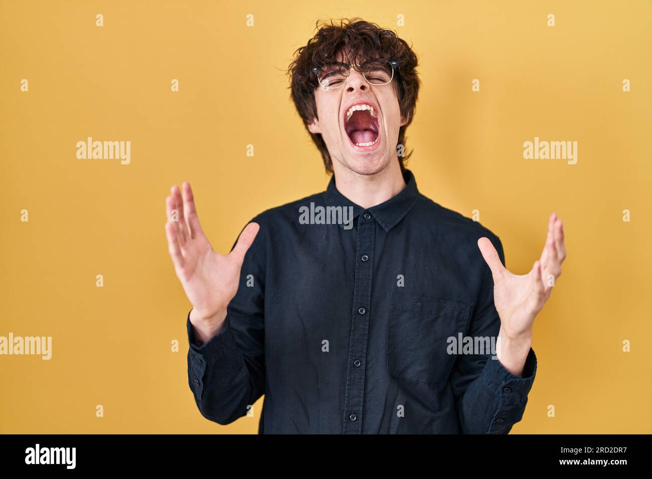 Young man wearing glasses over yellow background crazy and mad shouting ...