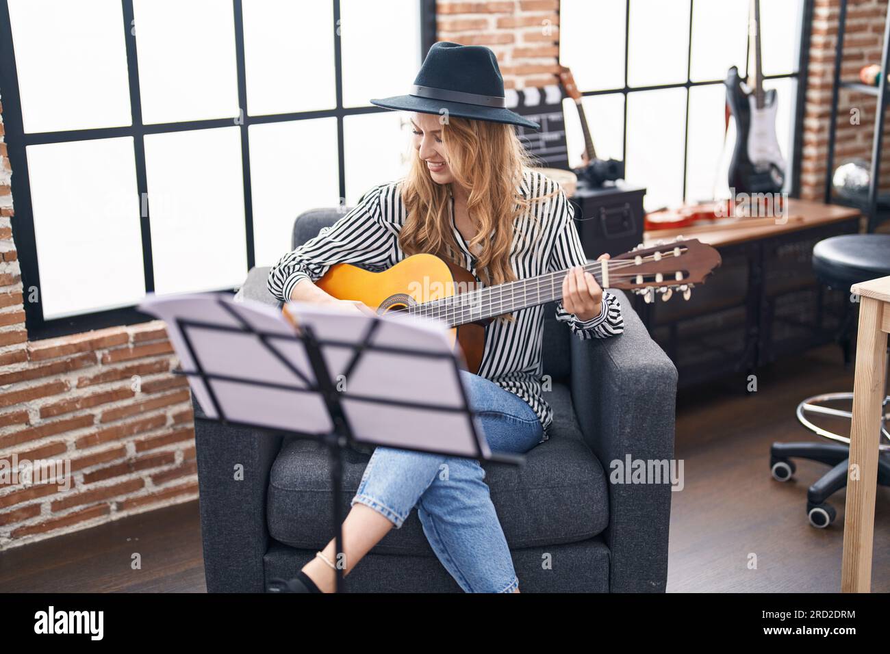 Young blonde woman musician playing classical guitar at music studio ...