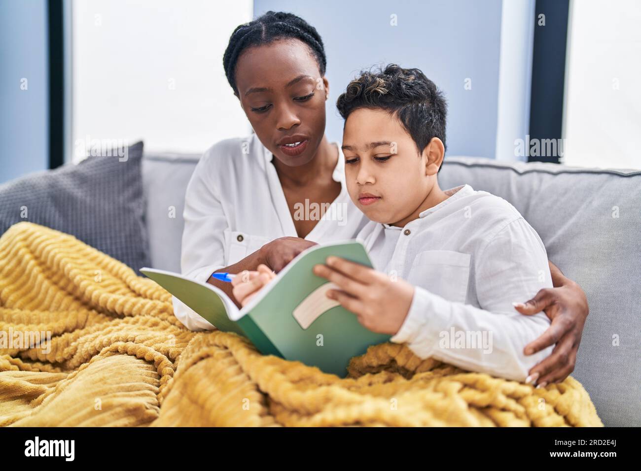 African american mother and son doing homework sitting on sofa at home ...