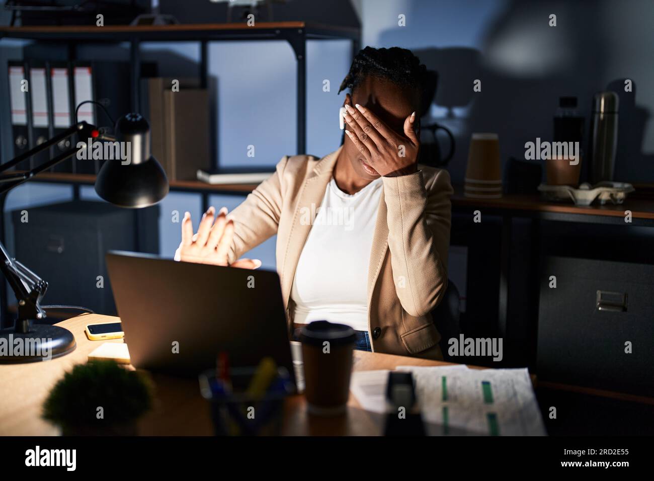Beautiful black woman working at the office at night covering eyes with ...