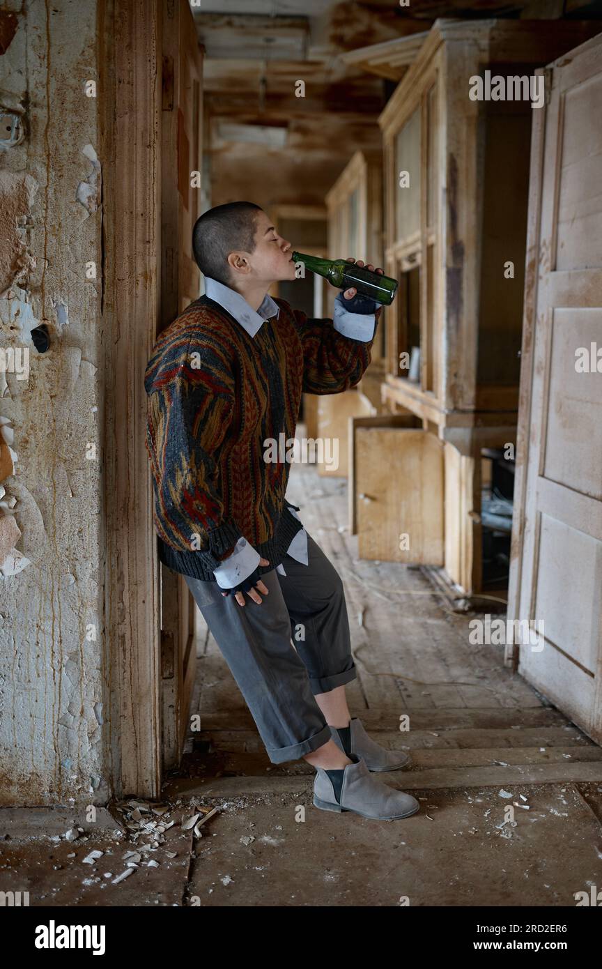 Homeless woman drinking beer from bottle living in abandoned house ...
