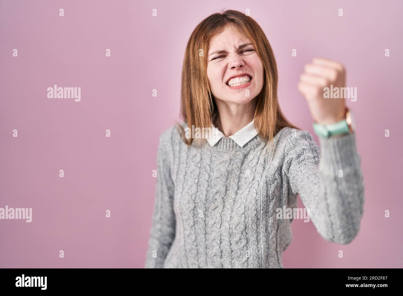 Beautiful woman standing over pink background angry and mad raising ...