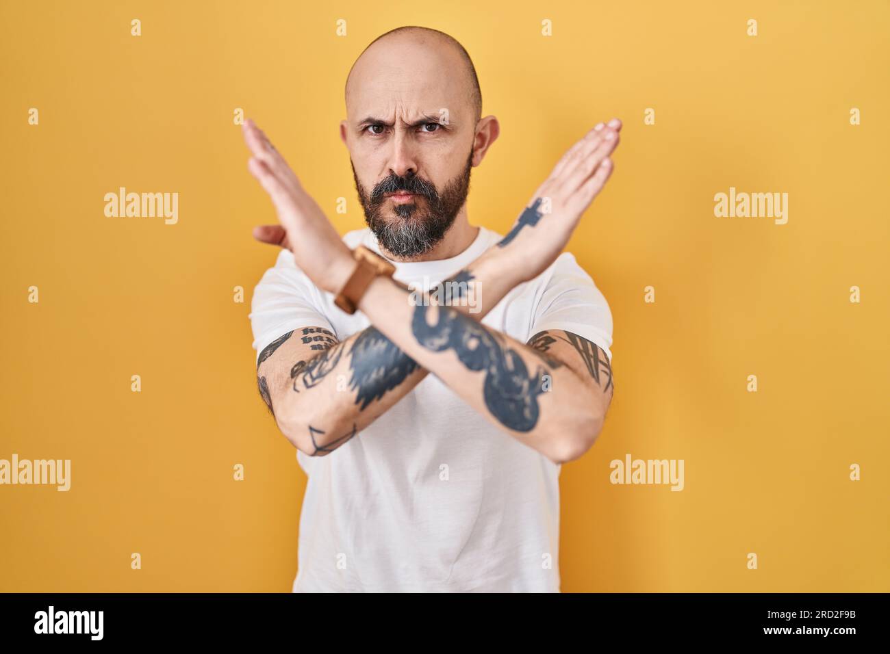 Young hispanic man with tattoos standing over yellow background ...