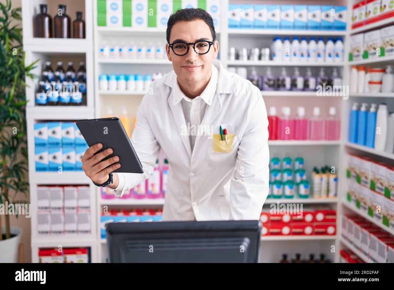 Young hispanic man pharmacist using touchpad and computer at pharmacy ...