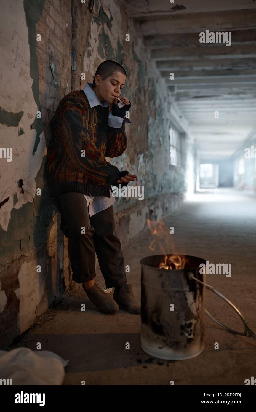 Poor homeless young teenager woman smoking while warming at bonfire ...