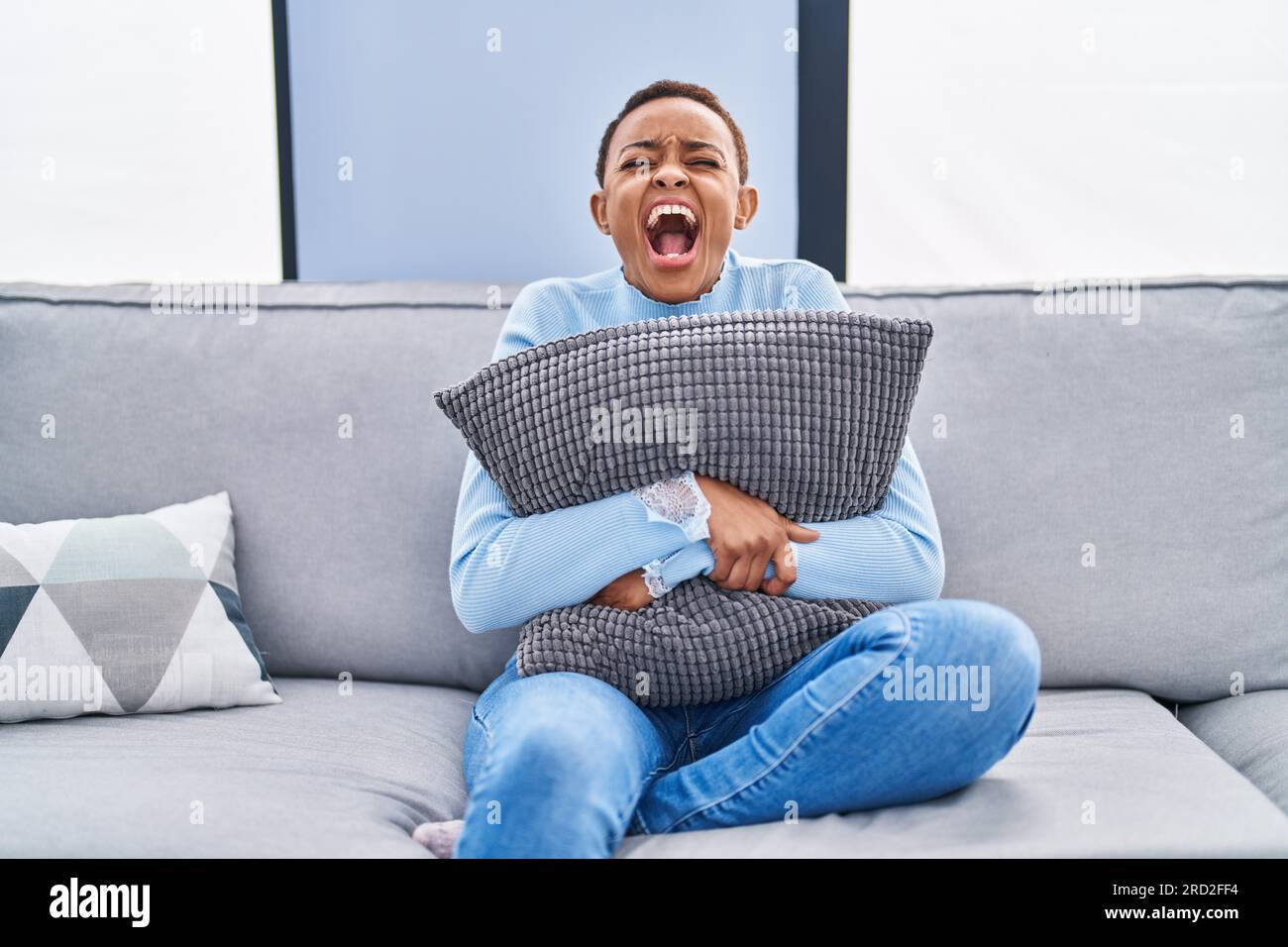 African american woman sitting on the sofa at home hugging pillow angry ...