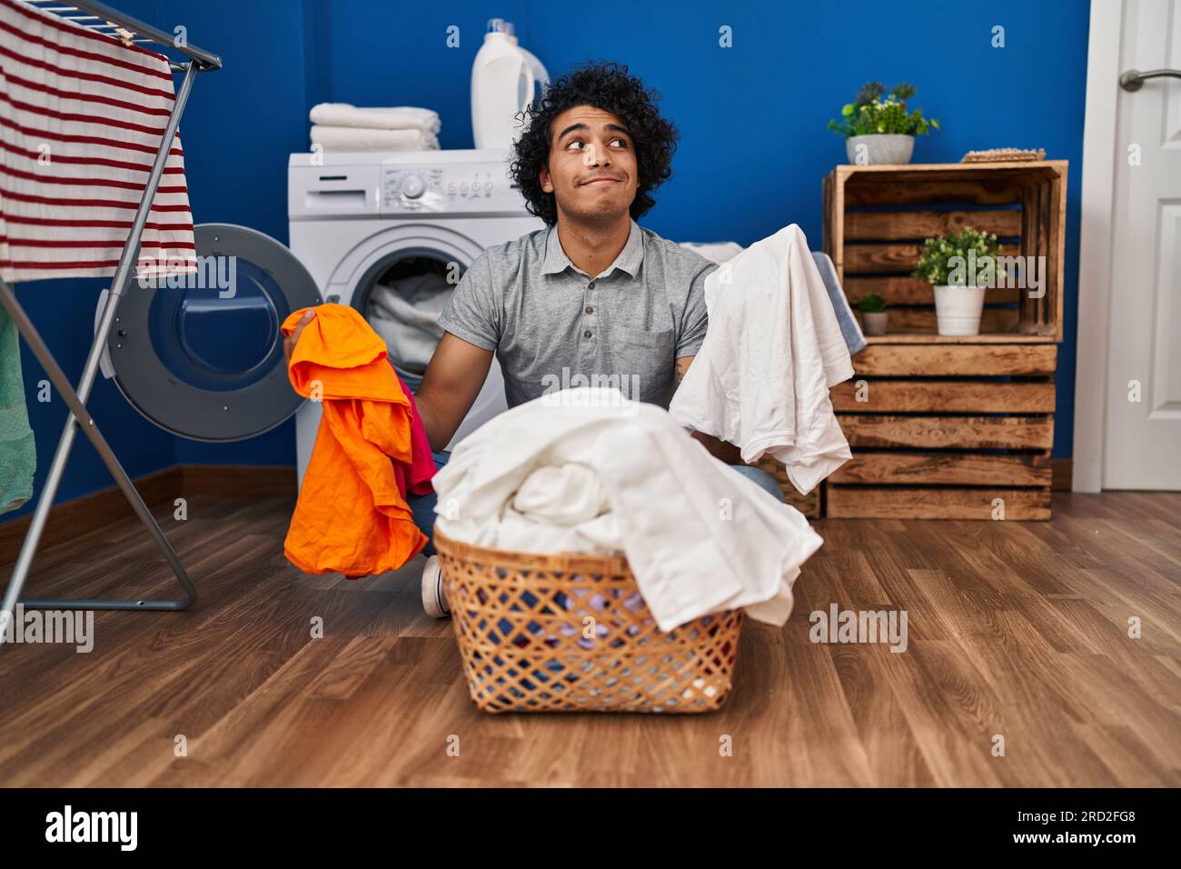 Hispanic man with curly hair doing laundry at laundry room smiling ...