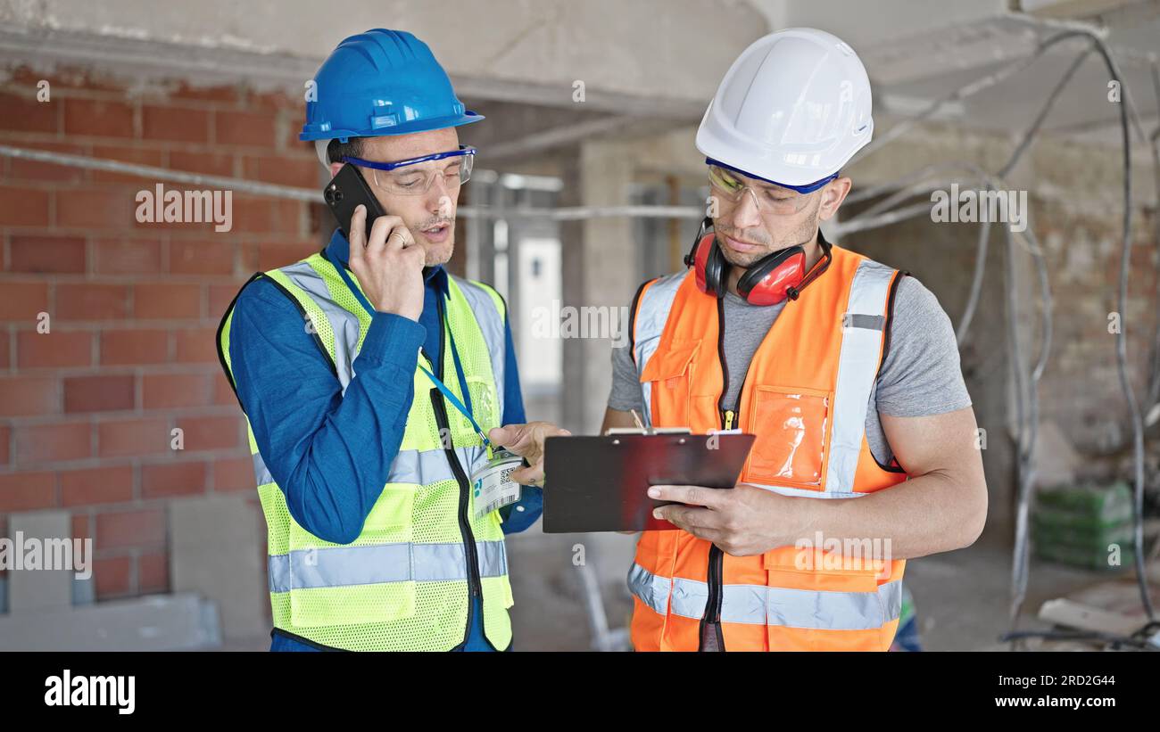 Two men builders writing document talking on smartphone at construction ...