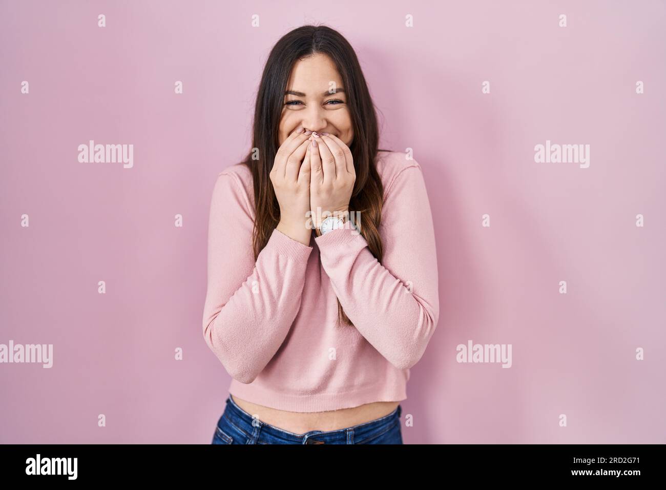 Young brunette woman standing over pink background laughing and ...