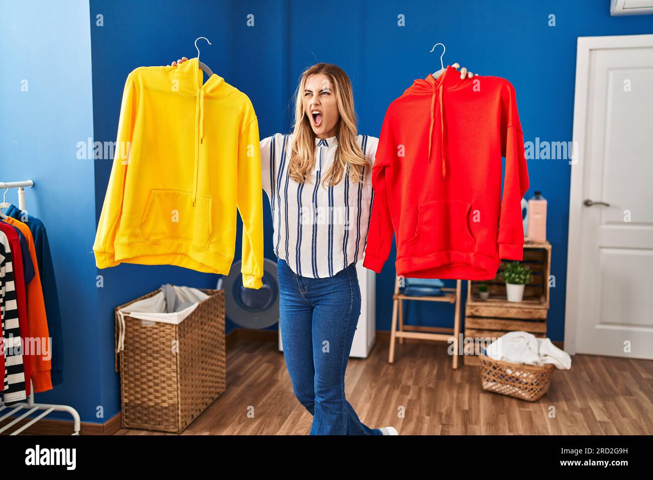 Young blonde woman holding clean laundry on hangers angry and mad ...