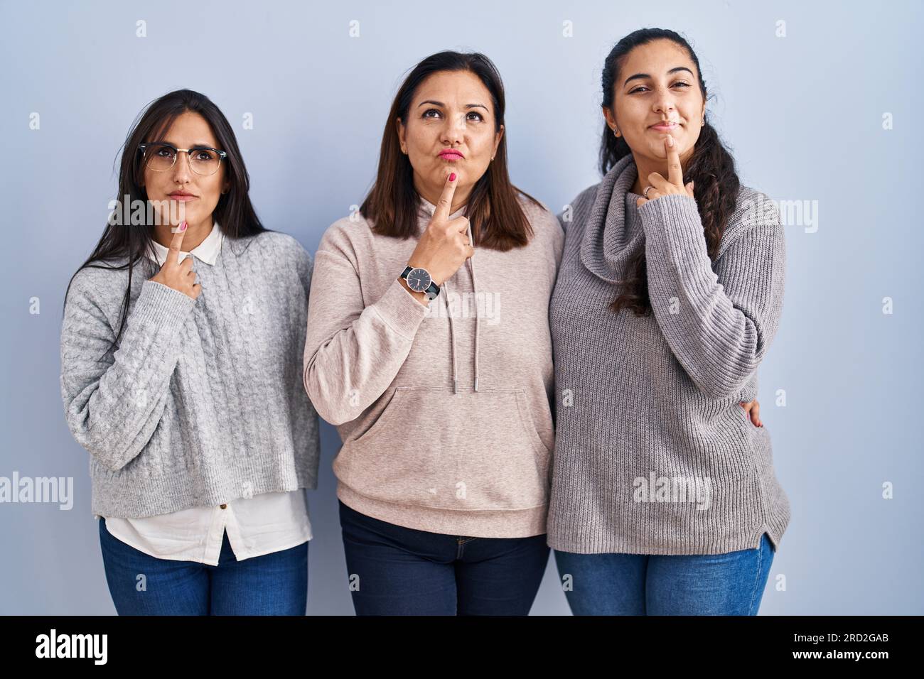 Mother and two daughters standing over blue background thinking ...