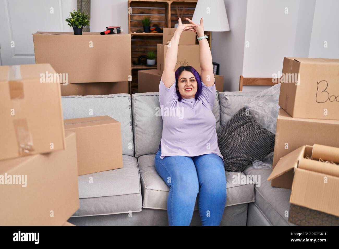 Young beautiful plus size woman sitting on sofa stretching arms at new ...
