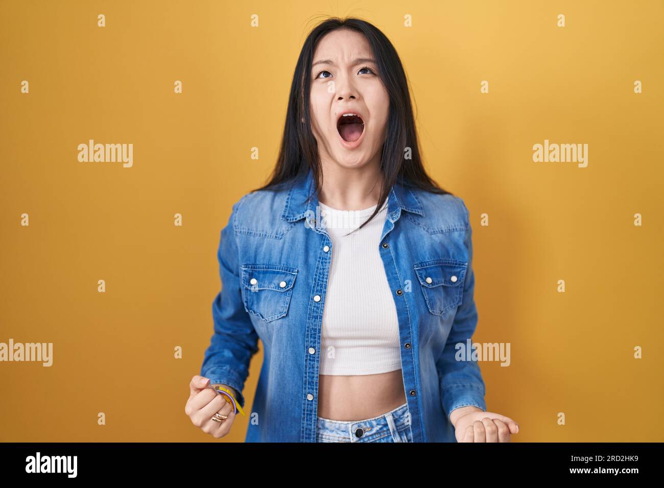 Young asian woman standing over yellow background angry and mad ...