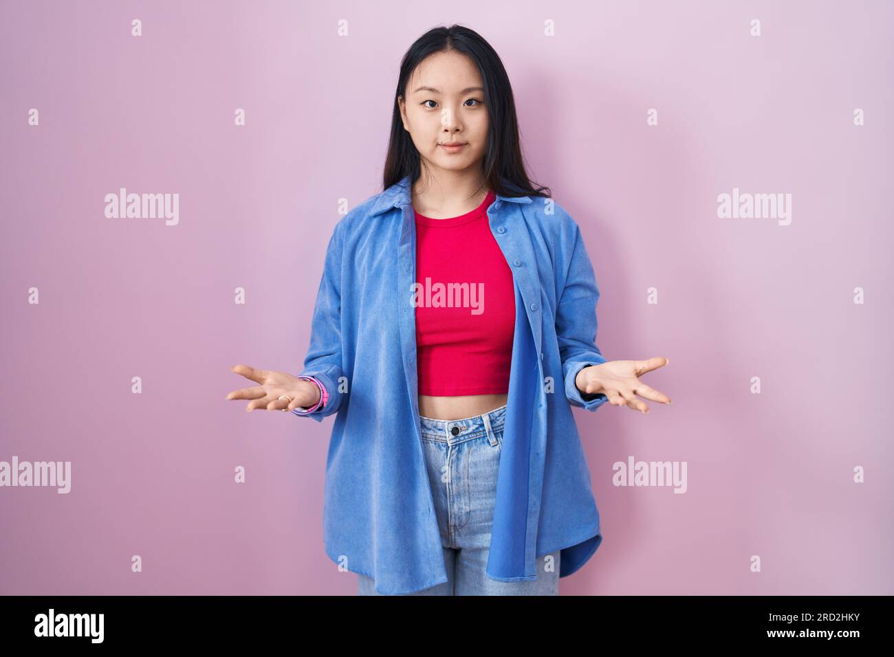 Young asian woman standing over pink background clueless and confused ...
