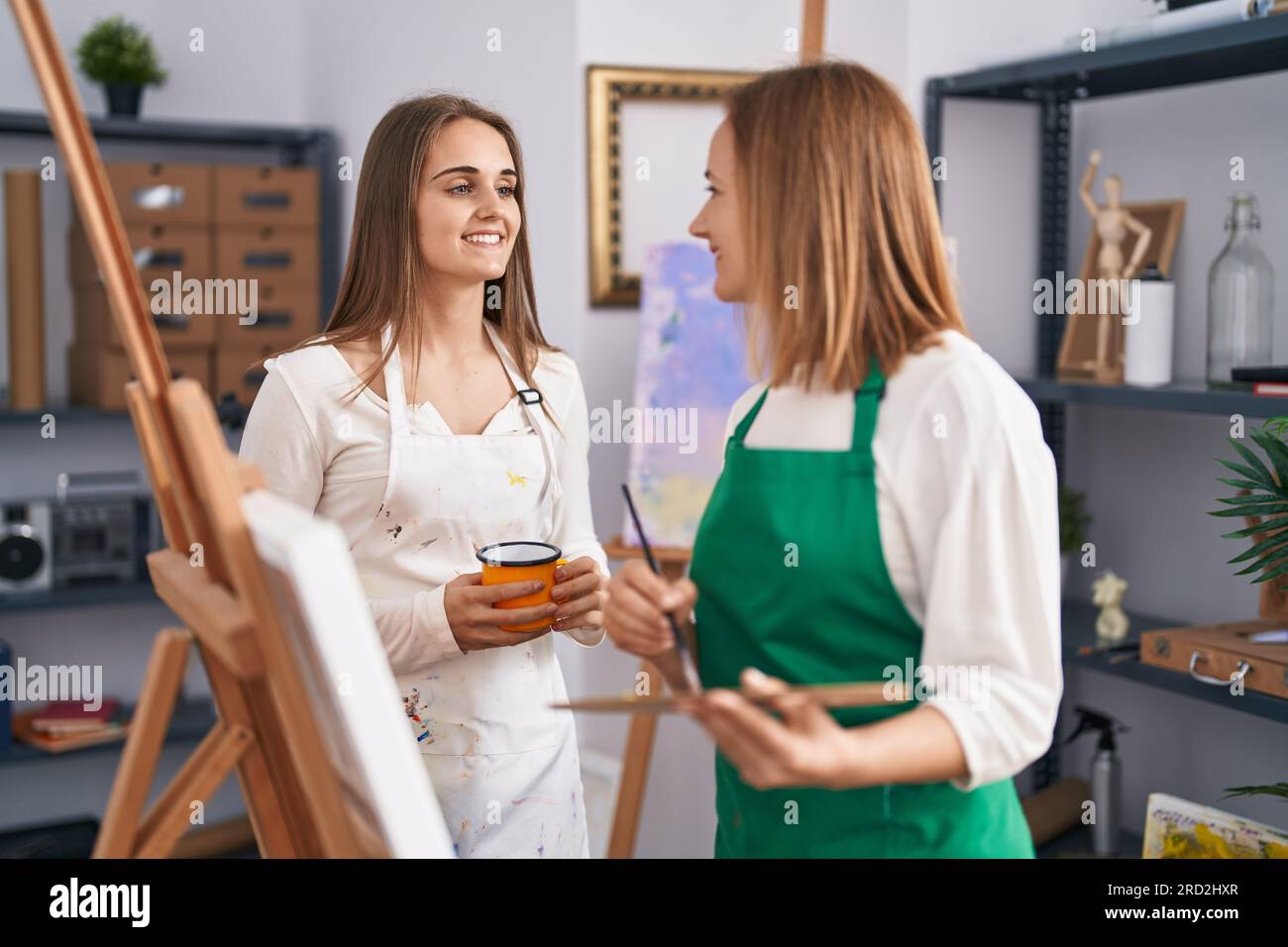 Two women artists smiling confident drinking coffee drawing at art ...