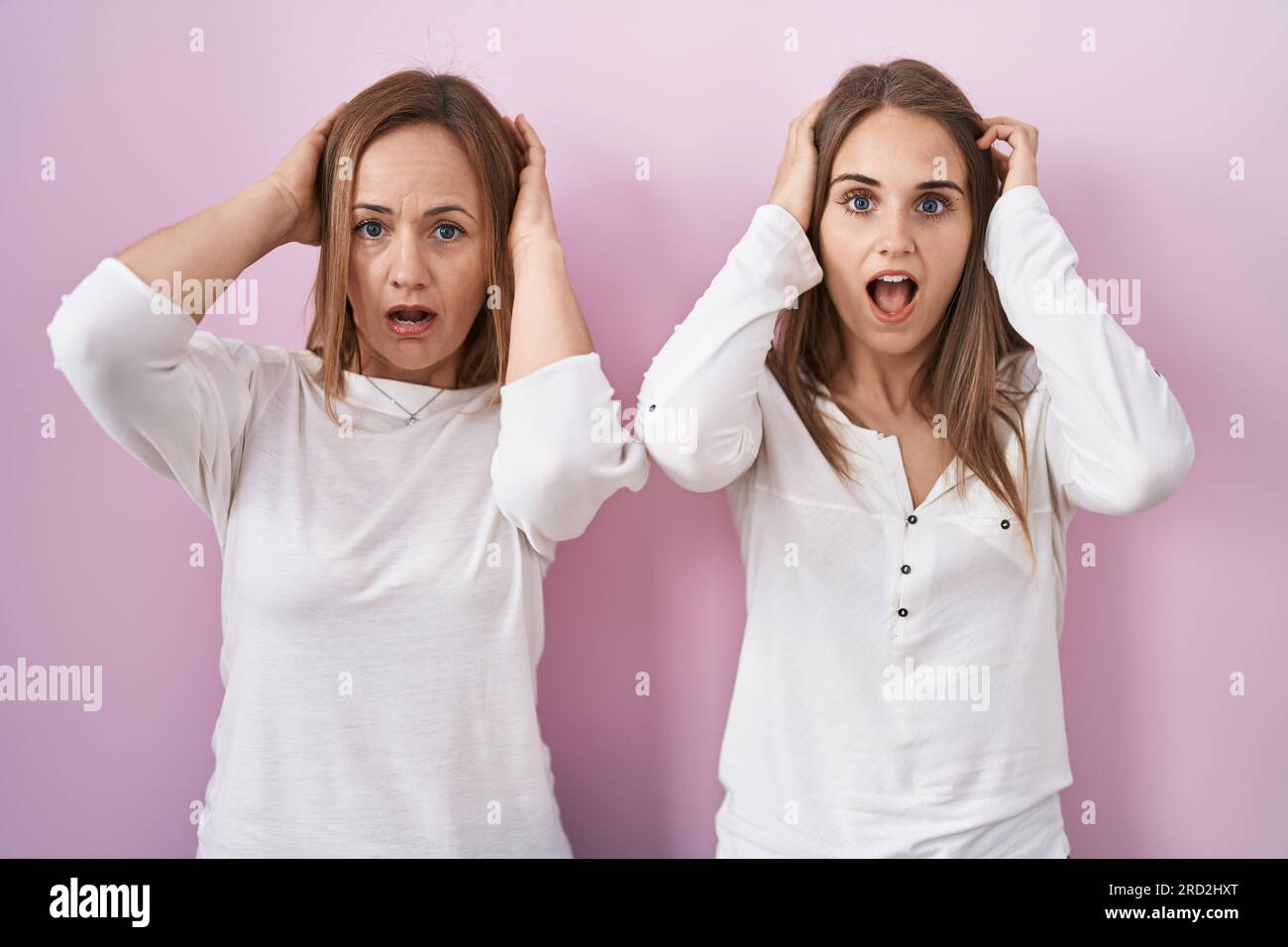 Middle age mother and young daughter standing over pink background ...