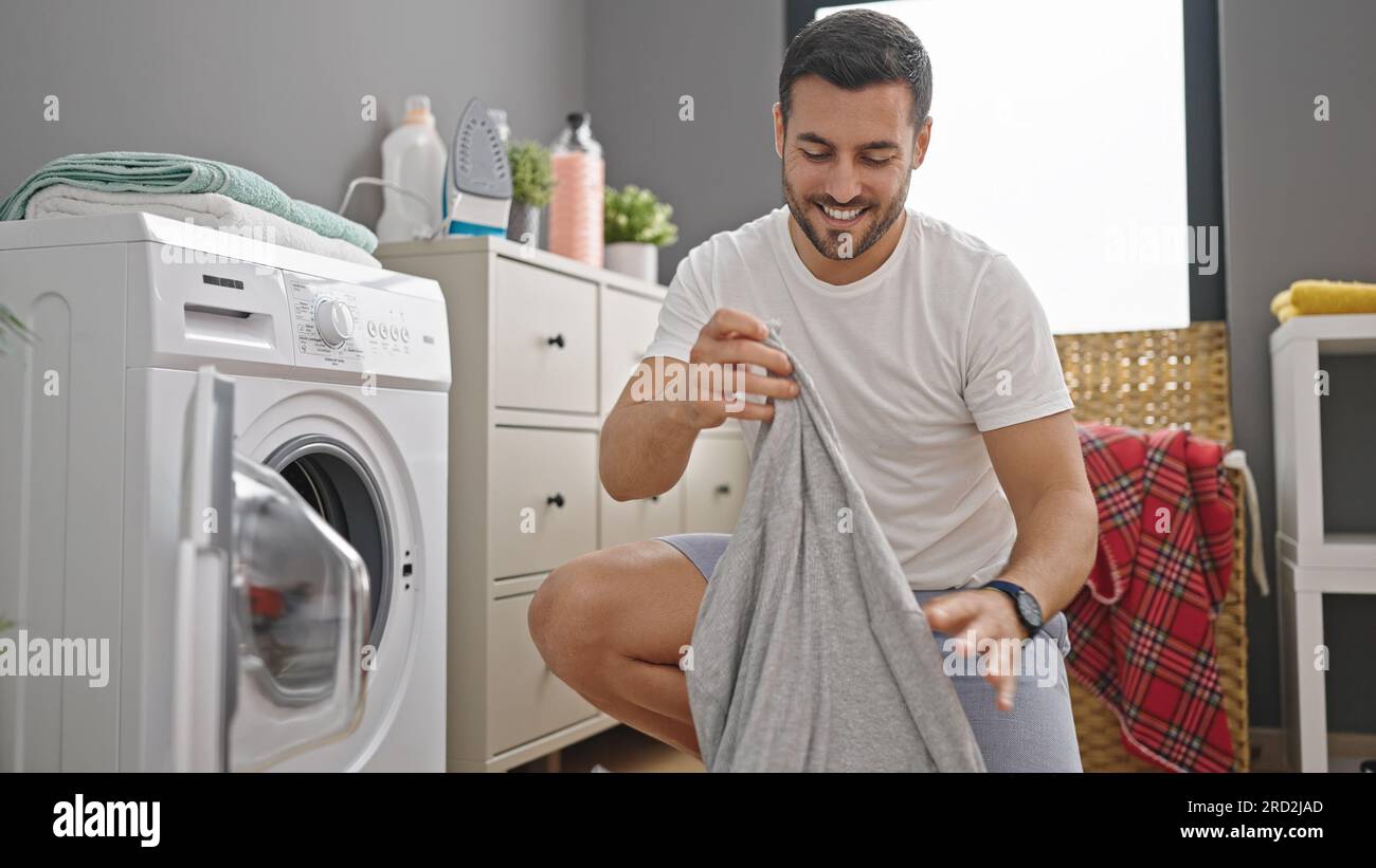 Young hispanic man smiling confident washing clothes at laundry room ...
