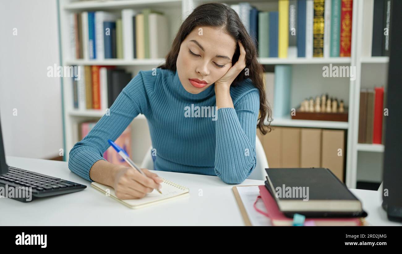 Young beautiful hispanic woman student writing notes tired at ...