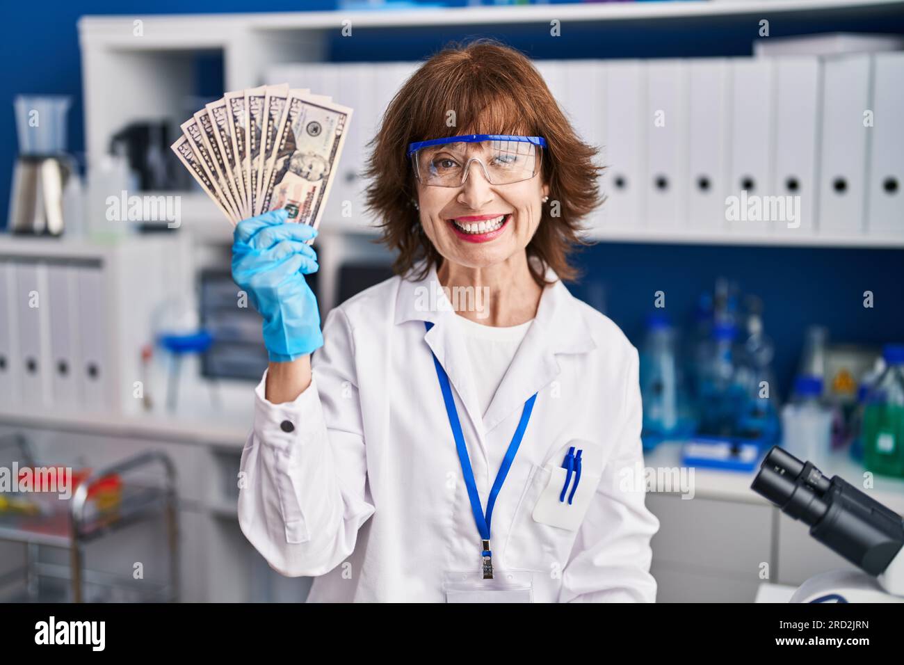 Middle age woman working at scientist laboratory holding money looking ...