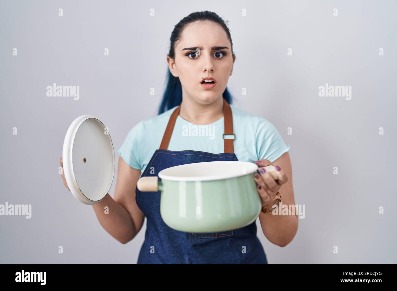 Young modern girl with blue hair wearing apron holding cooking pot in ...