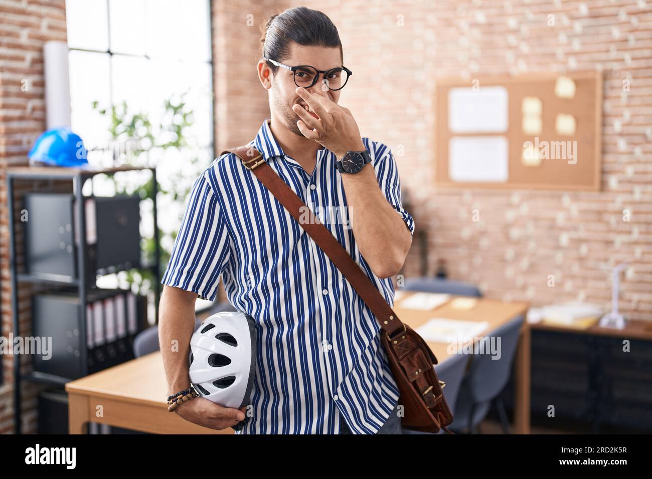 Hispanic man with long hair working at the office holding bike helmet ...
