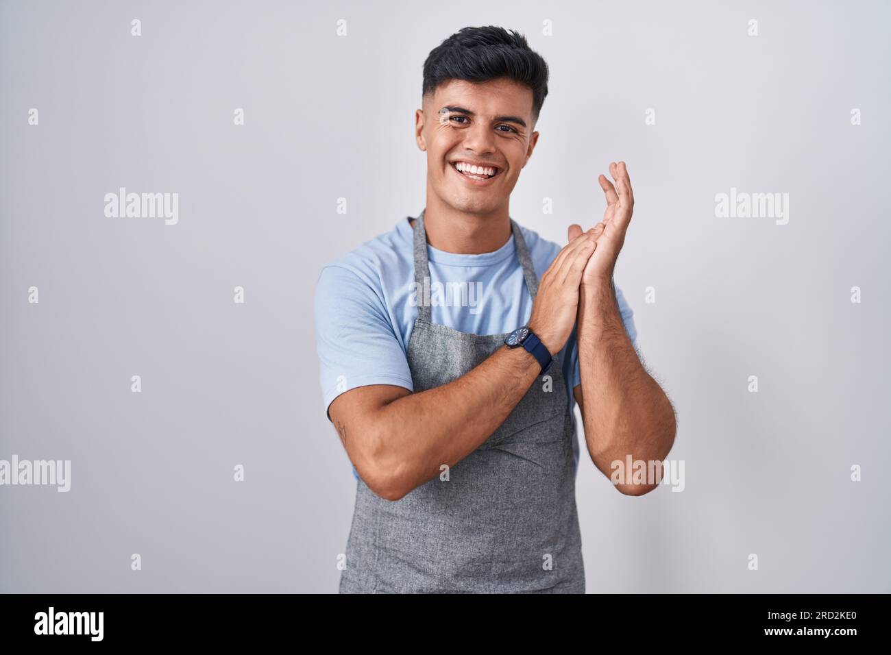 Hispanic young man wearing apron over white background clapping and ...