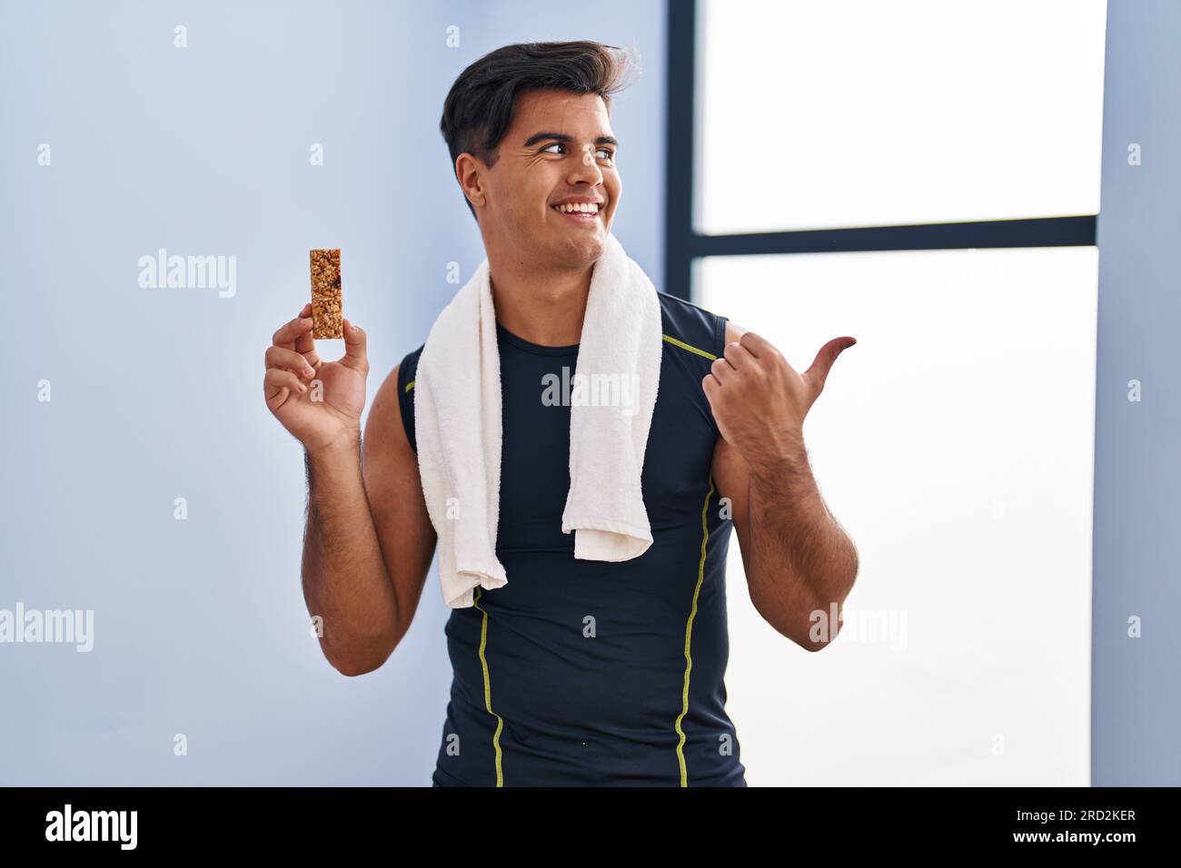 Hispanic man eating protein bar as healthy energy snack pointing thumb ...