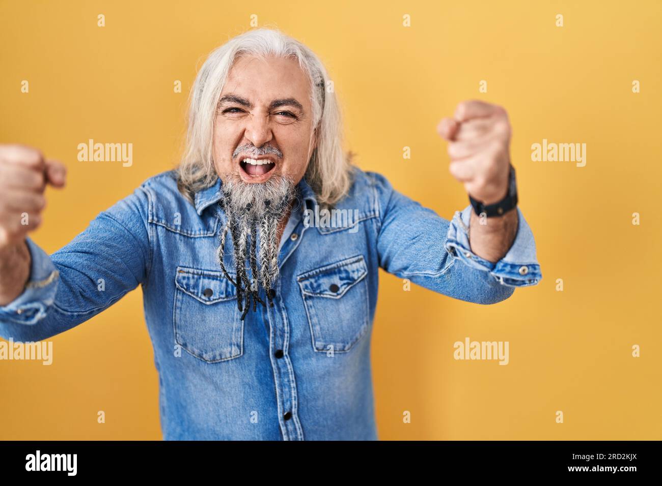 Middle age man with grey hair standing over yellow background angry and ...