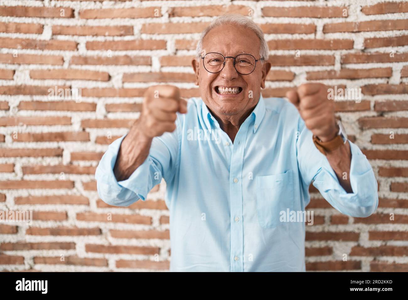 Senior man with grey hair standing over bricks wall angry and mad ...