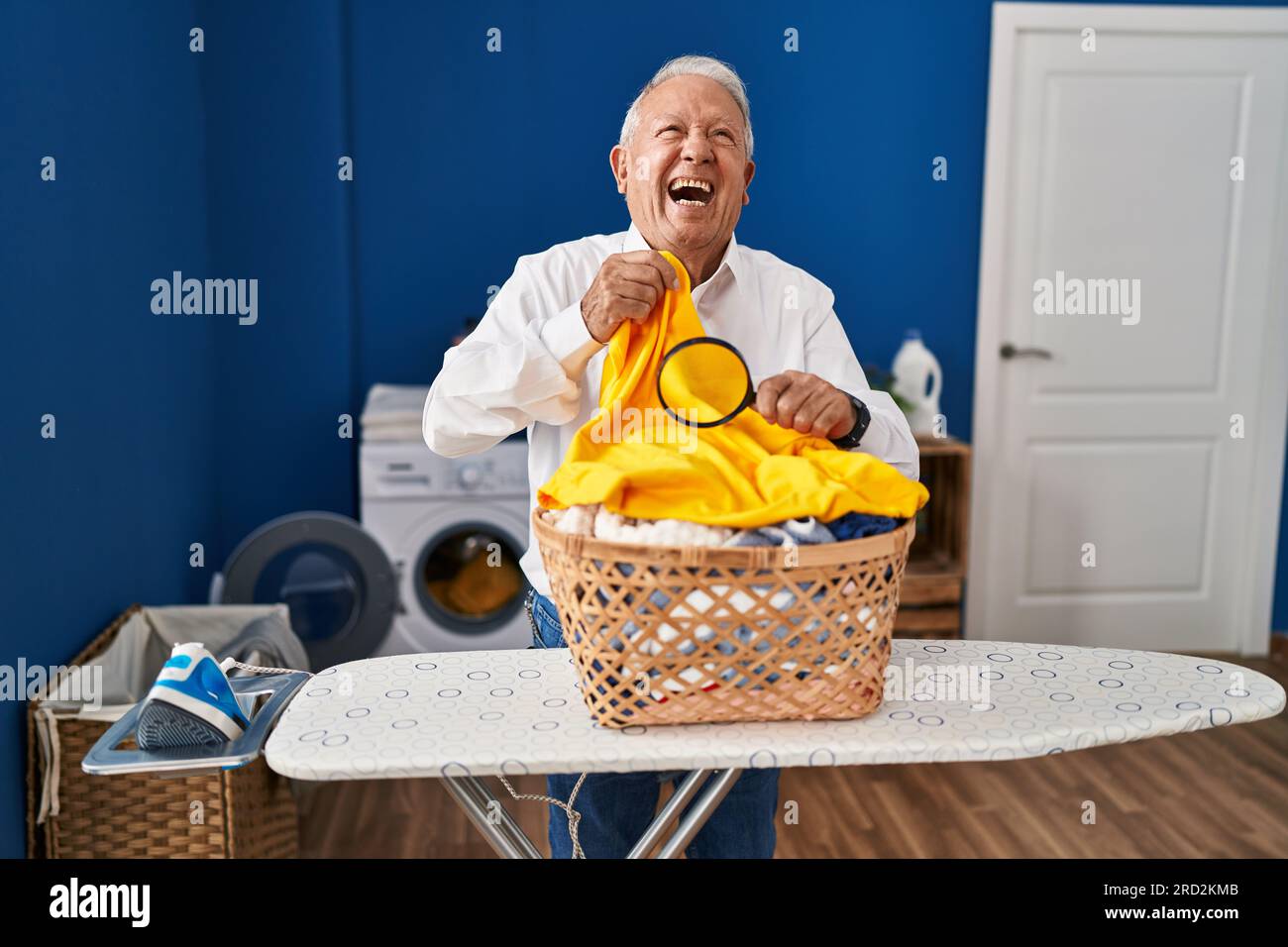Senior man with grey hair holding magnifying glass looking for stain at ...