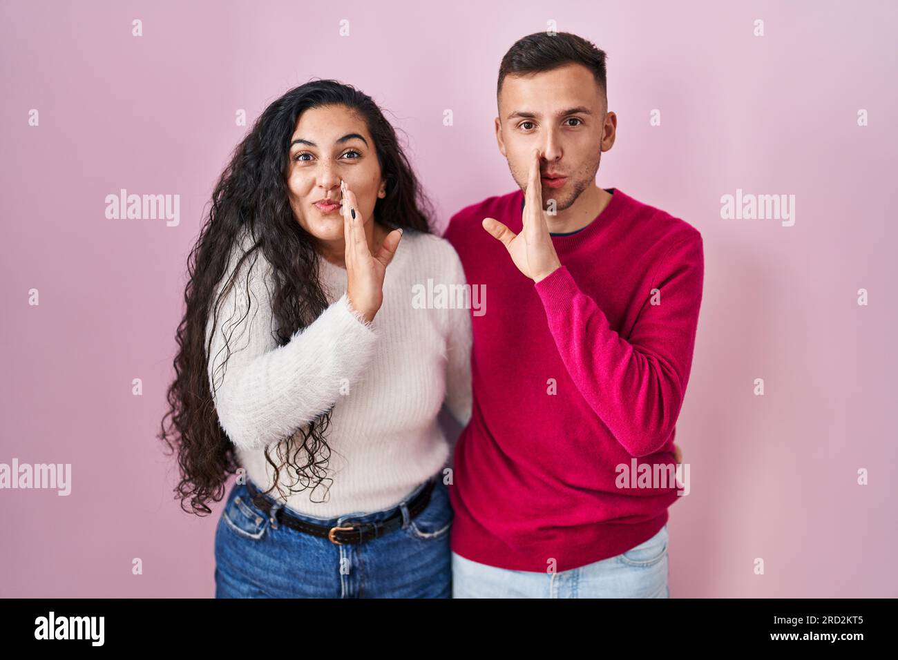 Young hispanic couple standing over pink background hand on mouth ...