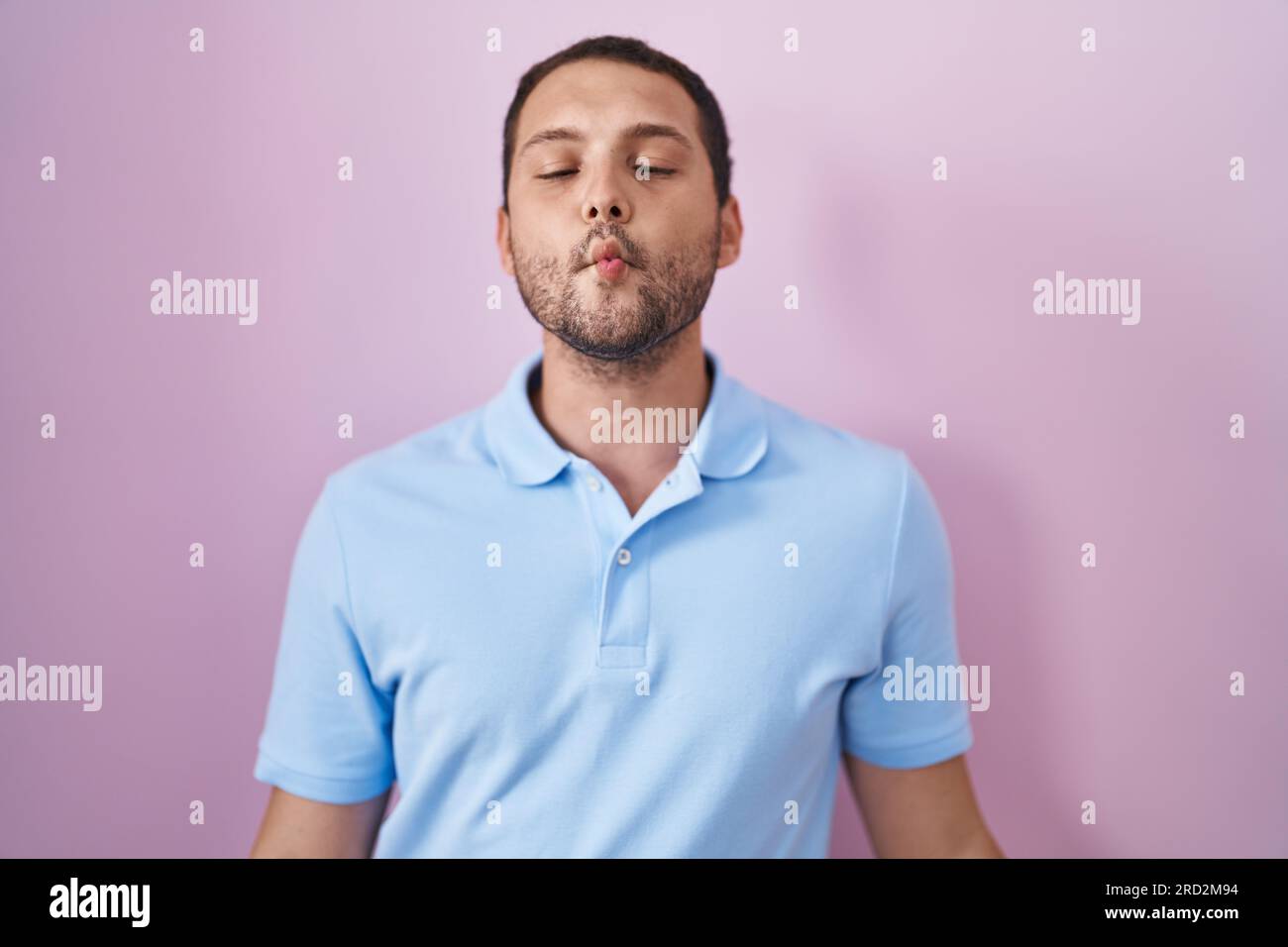 Hispanic man standing over pink background making fish face with lips ...