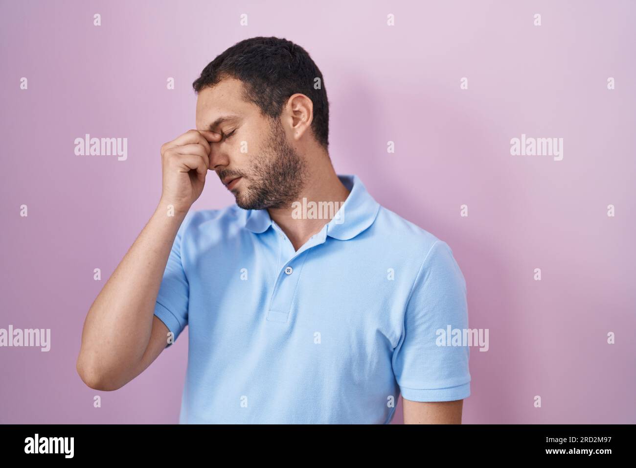 Hispanic man standing over pink background tired rubbing nose and eyes ...
