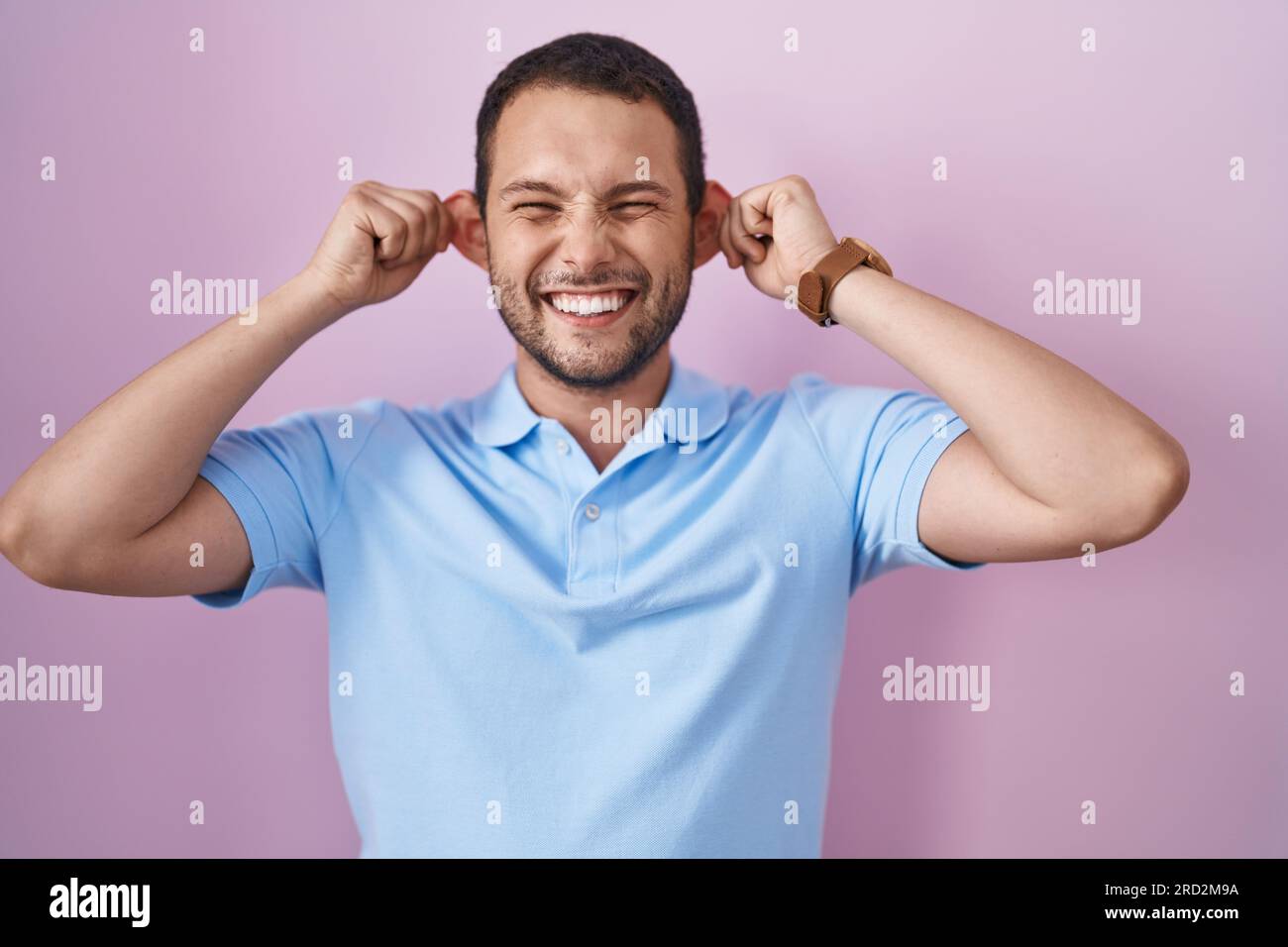 Hispanic man standing over pink background smiling pulling ears with ...
