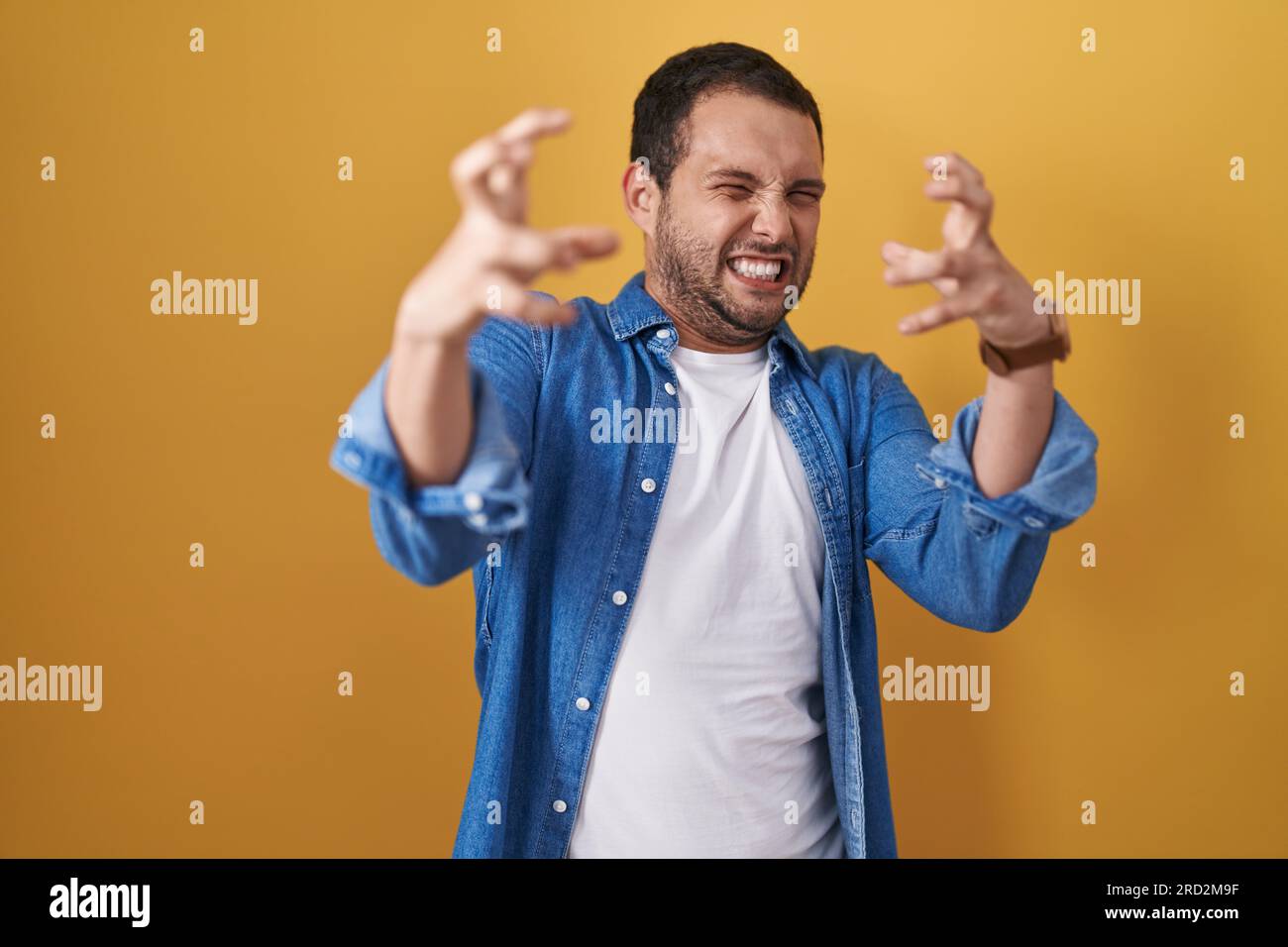 Hispanic man standing over yellow background shouting frustrated with ...