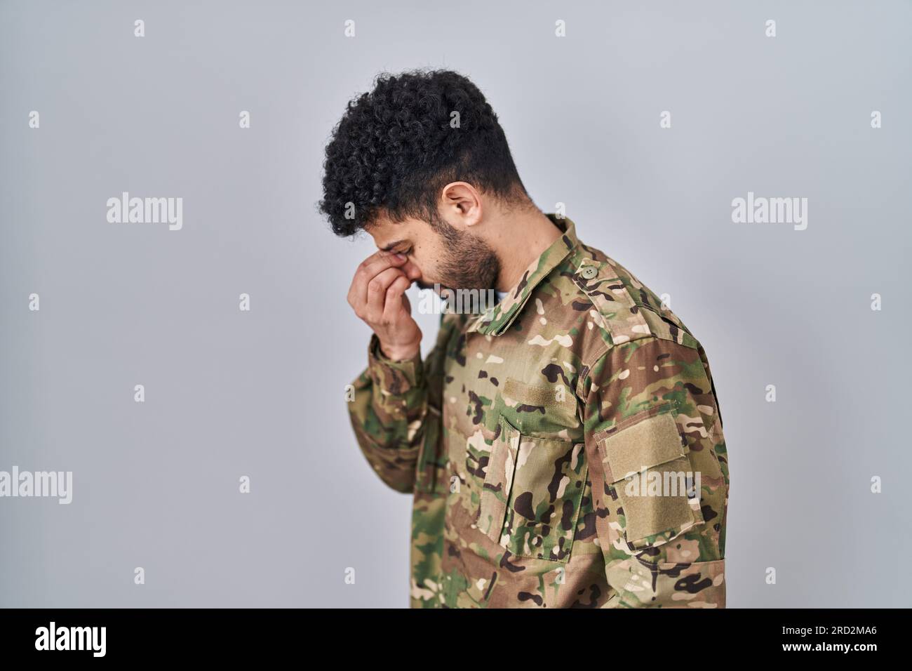 Arab man wearing camouflage army uniform tired rubbing nose and eyes ...