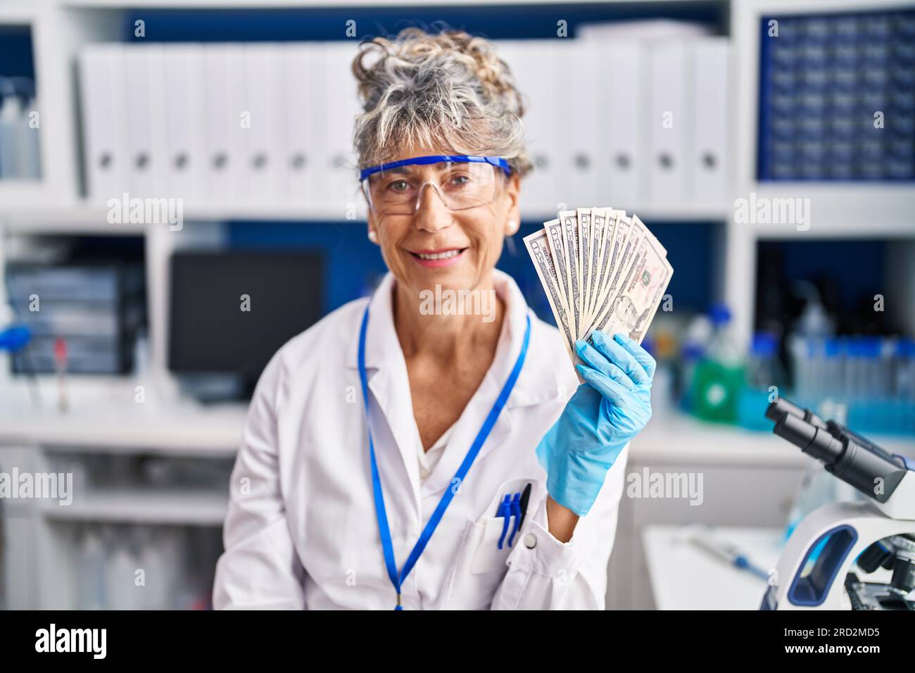 Middle age woman working at scientist laboratory holding dollars ...
